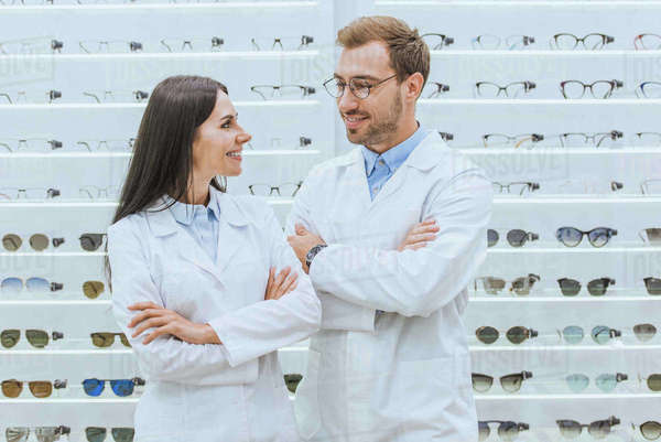 Happy professional opticians in white coats posing with crossed arms in ...