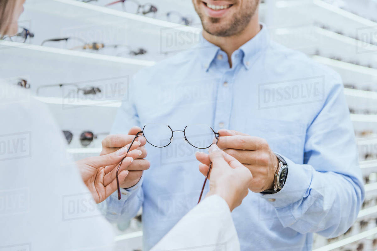 Cropped image of female oculist giving eyeglasses to young man in ...