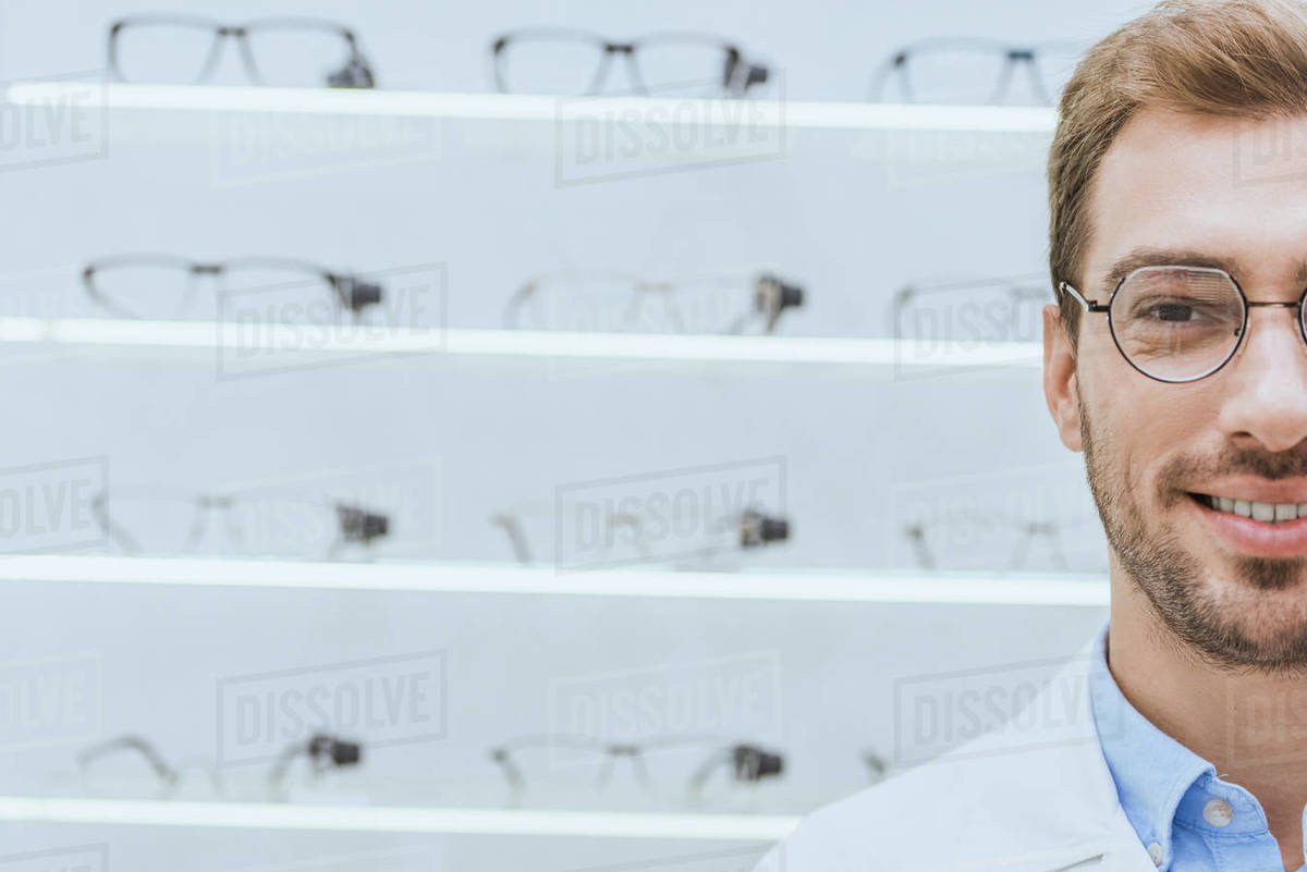 Professional handsome optician in glasses standing at shelves in Optica ...
