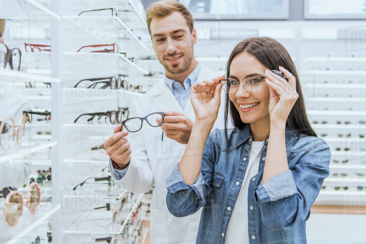 Happy woman choosing eyeglasses while male oculist standing near with ...