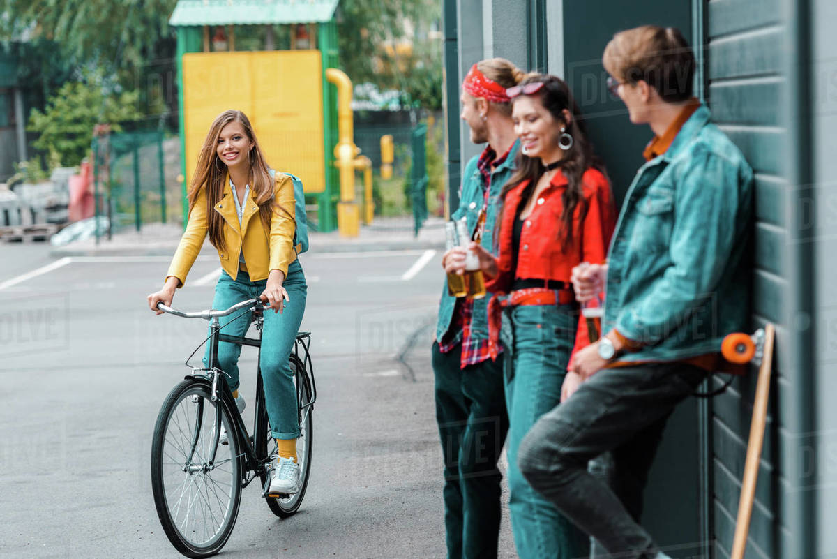 attractive stylish girl riding bike near friends with beer bottles on ...