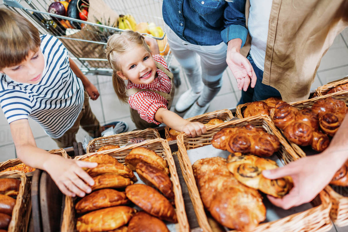 cropped shot of happy family with two kids choosing pastries in ...