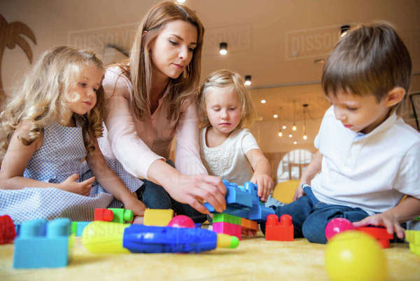 Educator and adorable kids playing with constructor in kindergarten ...