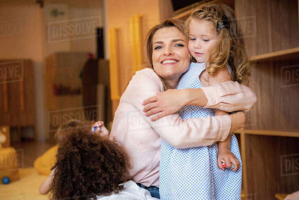 Smiling educator cuddling adorable kid in kindergarten - Royalty-free ...