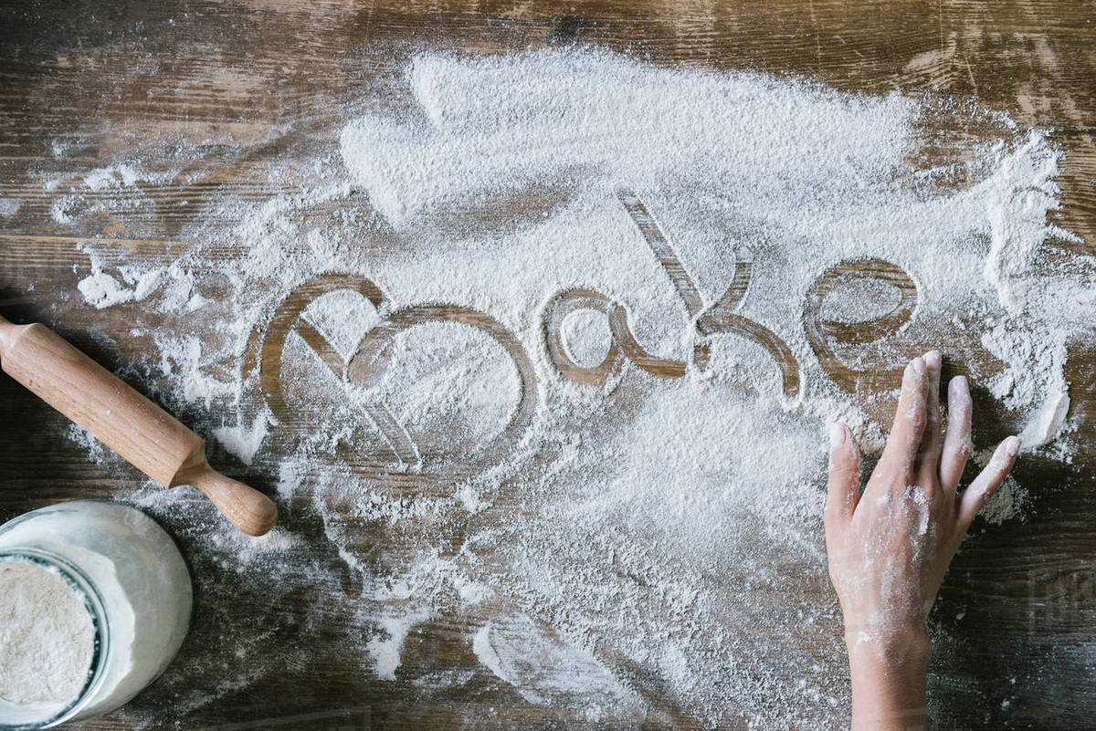 Cropped shot of woman writing word BAKE with finger on rustic wooden ...