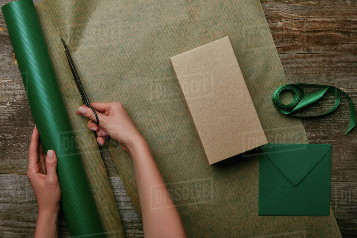 Partial view of woman cutting wrapping paper with scissors on wooden ...