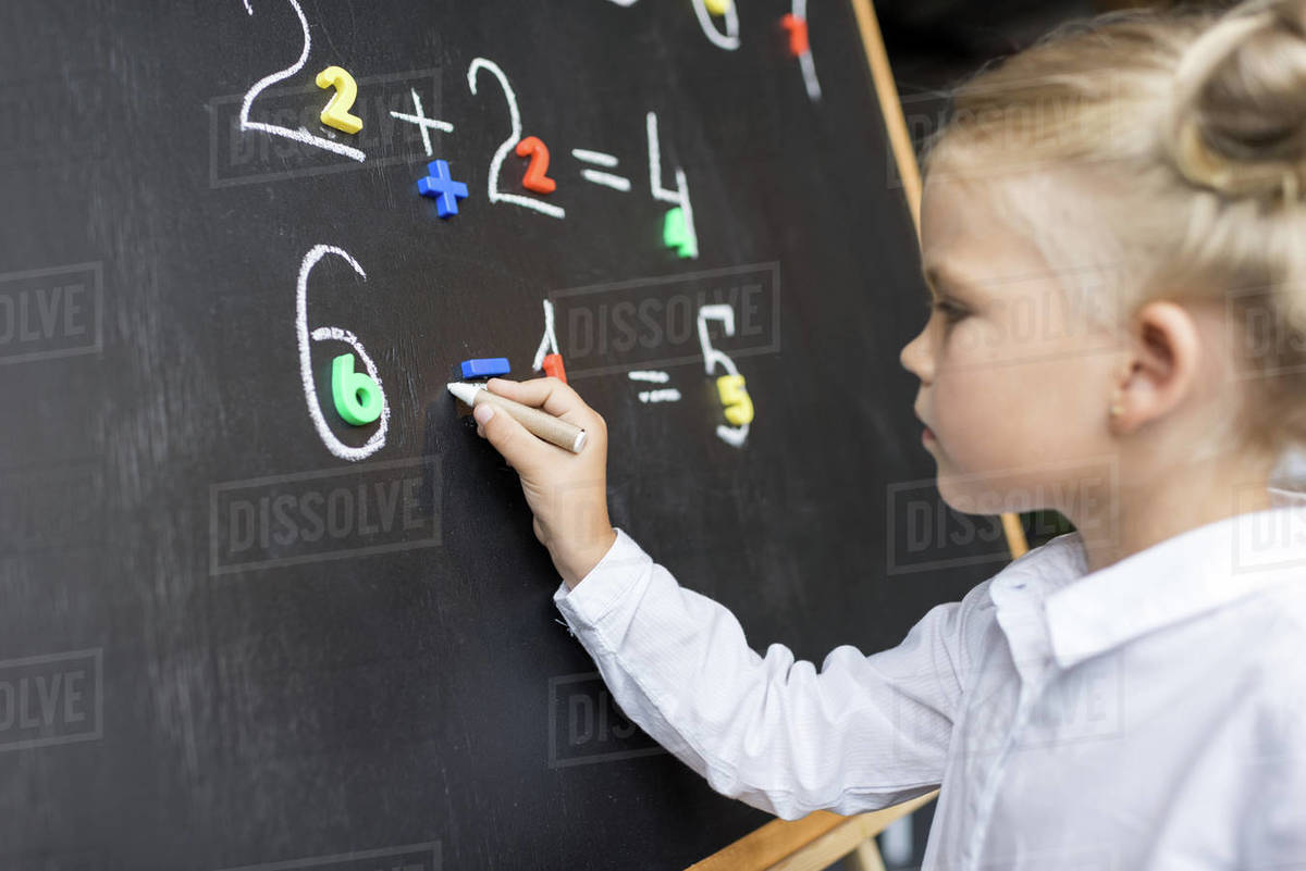 Focused elementary school student studying mathematics on blackboard ...