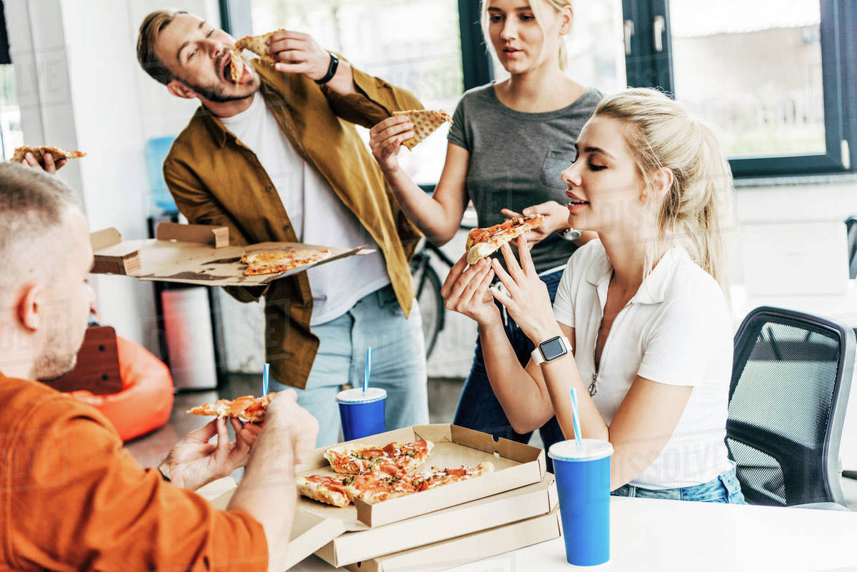 group of young entrepreneurs eating pizza for lunch together while ...