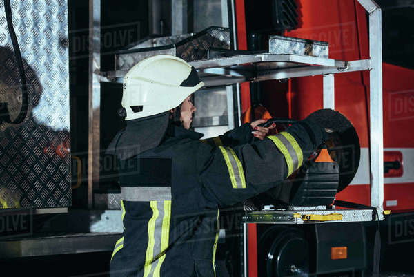 side view of female firefighter standing at equipment in truck at fire ...