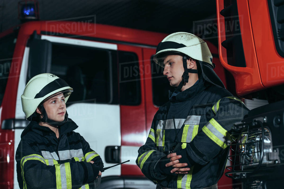 firefighters in fireproof uniform and helmets looking at each other at ...