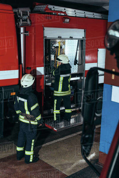 partial view of firefighters in fireproof uniform and helmets at fire ...