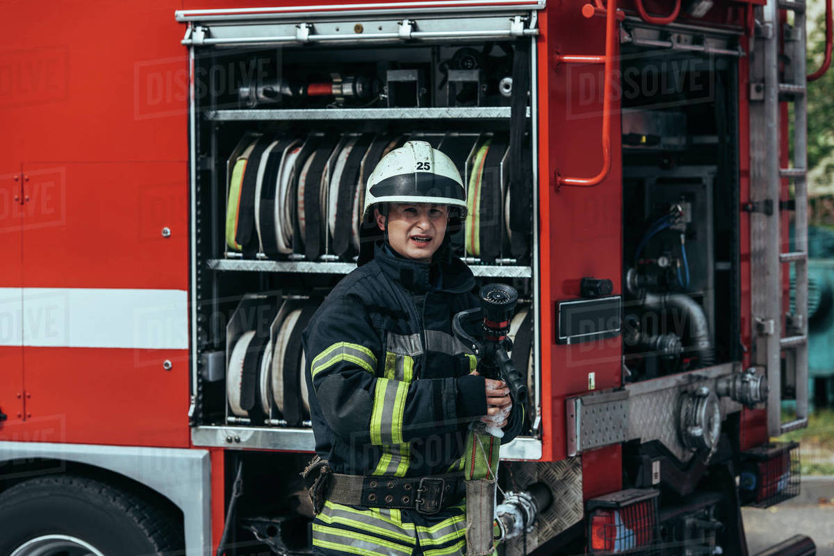 portrait of fireman in protective uniform and helmet standing at truck ...