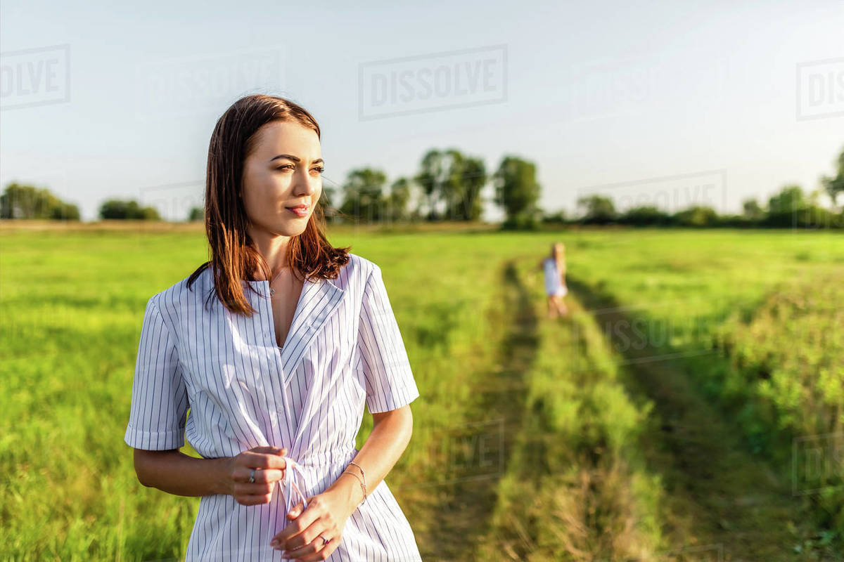 Attractive young woman on rural road in green field under sunset rays ...