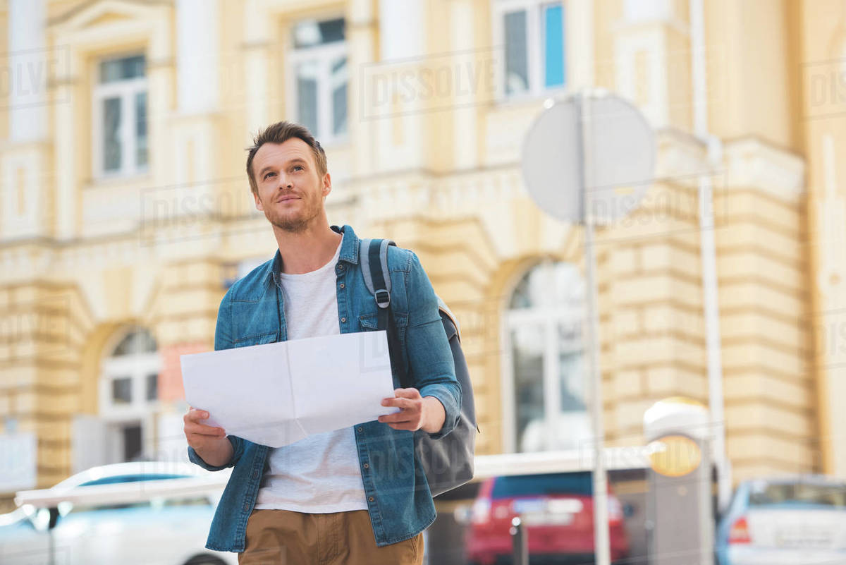 Portrait of smiling traveler with backpack and map on city street ...