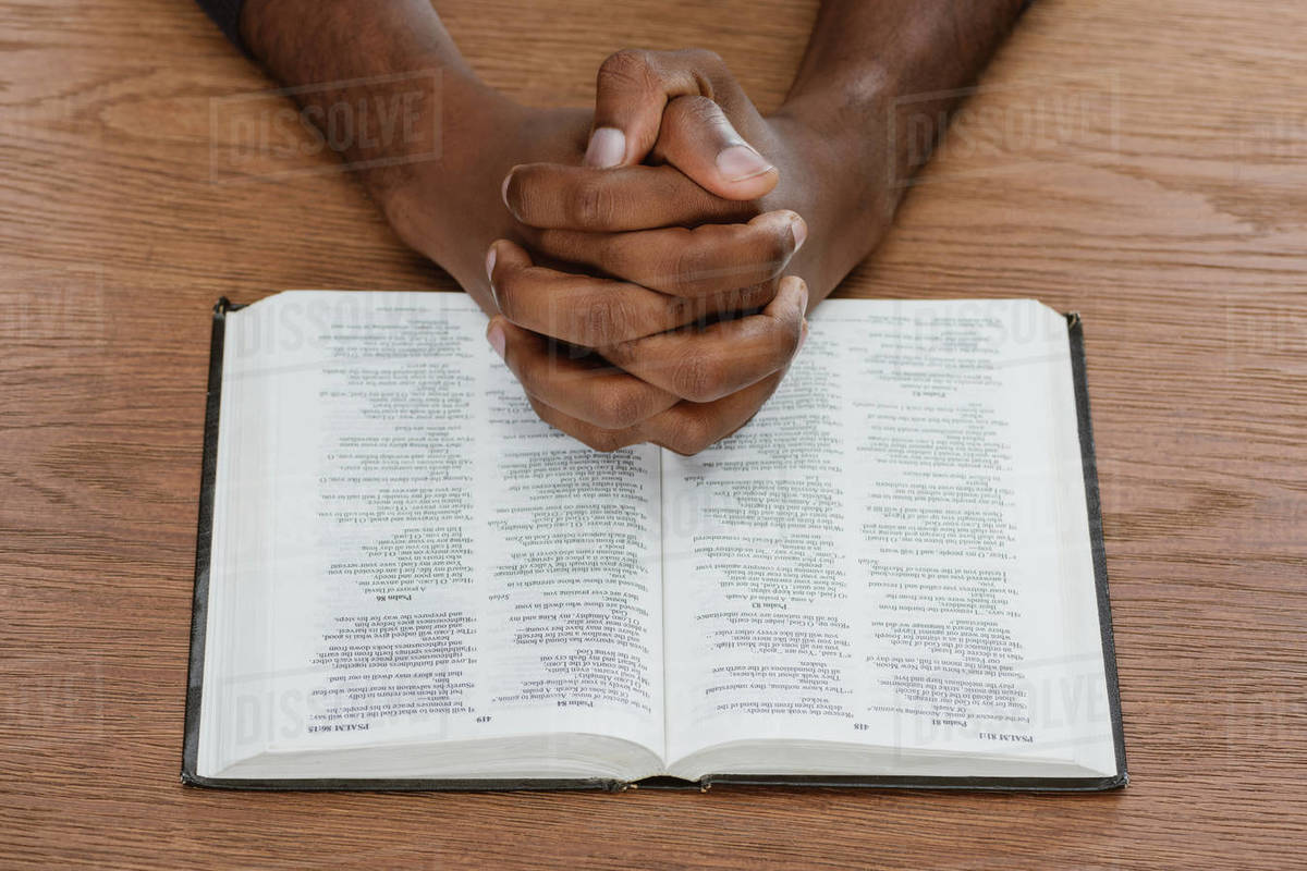 Cropped shot of African American man praying with holy bible on wooden ...
