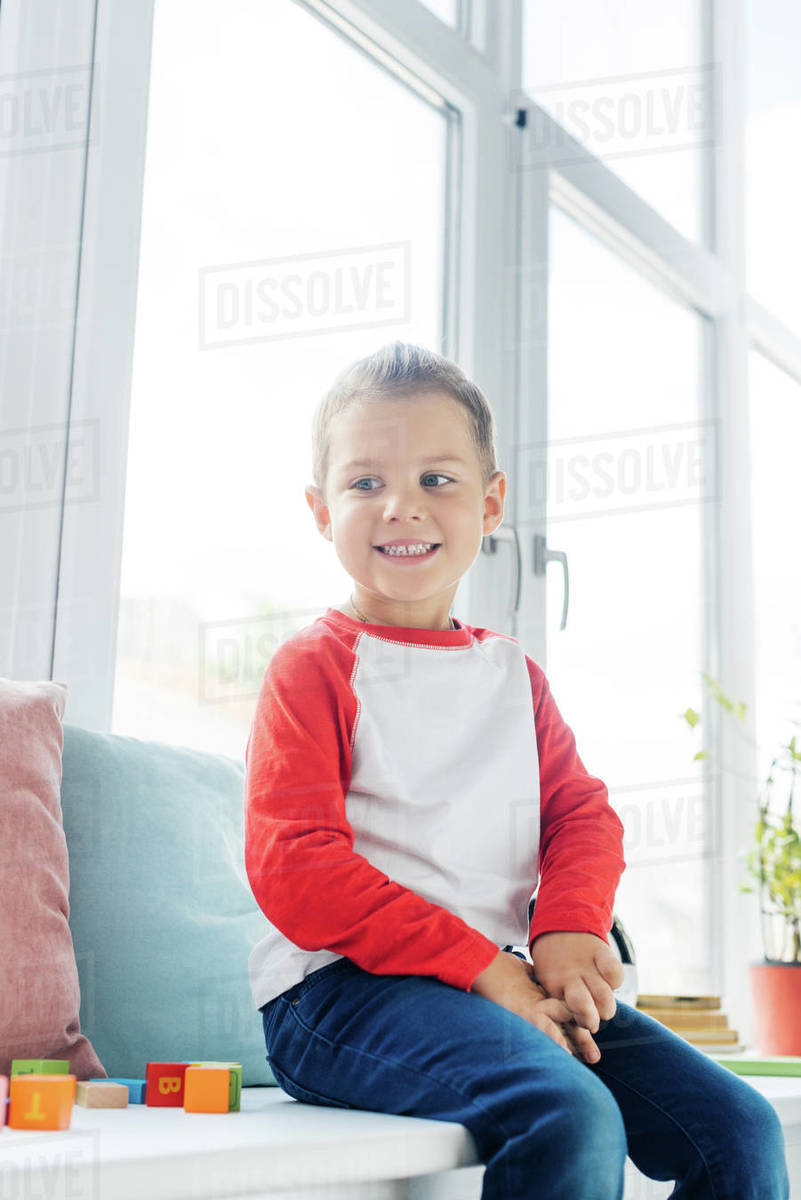Portrait of cute cheerful boy sitting at window at home - Stock Photo ...