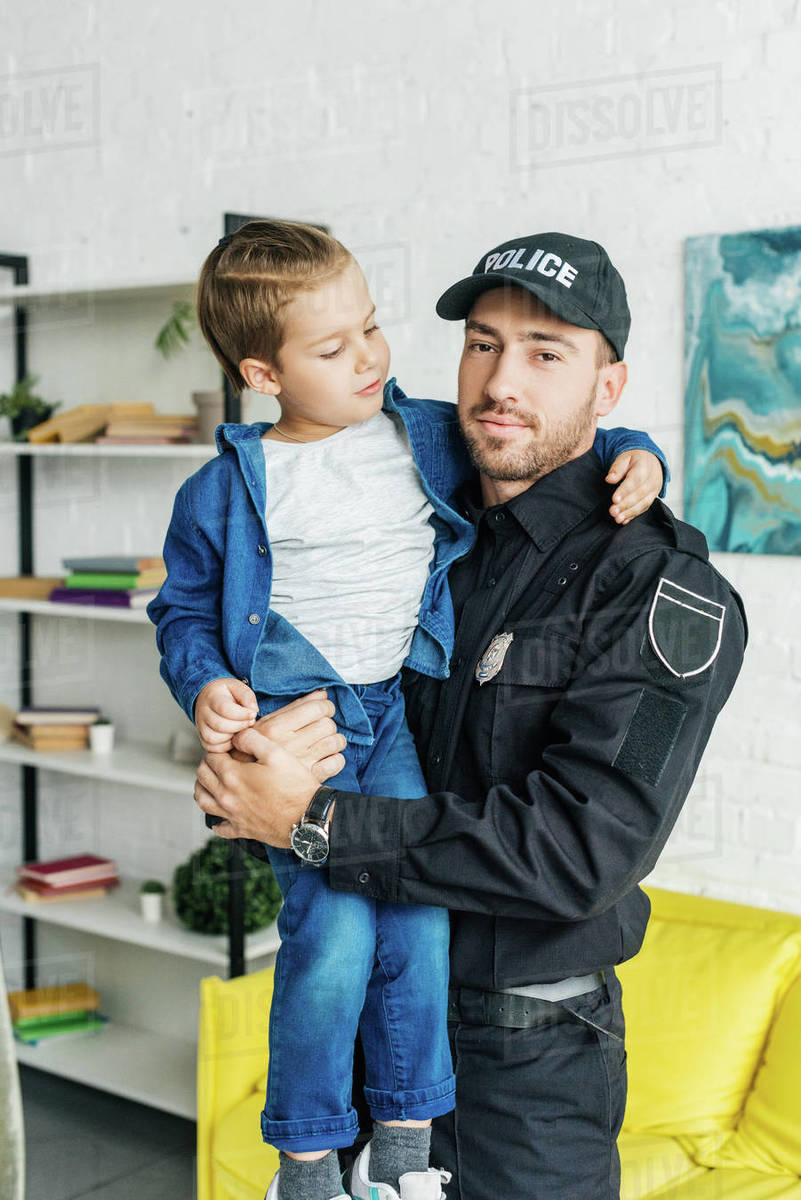 Handsome young father in police uniform carrying his little son and ...