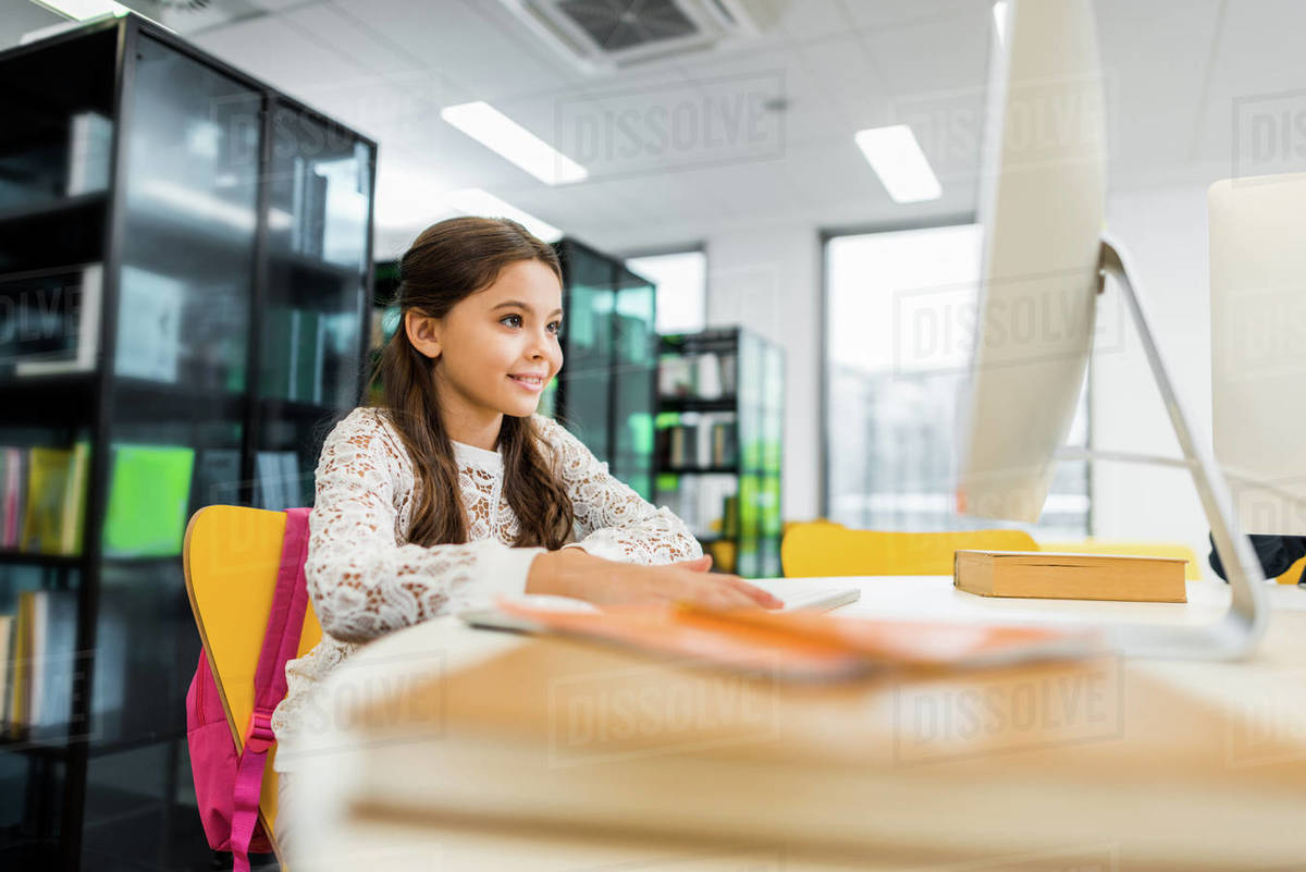 Adorable smiling schoolkid using desktop computer in library - Stock ...