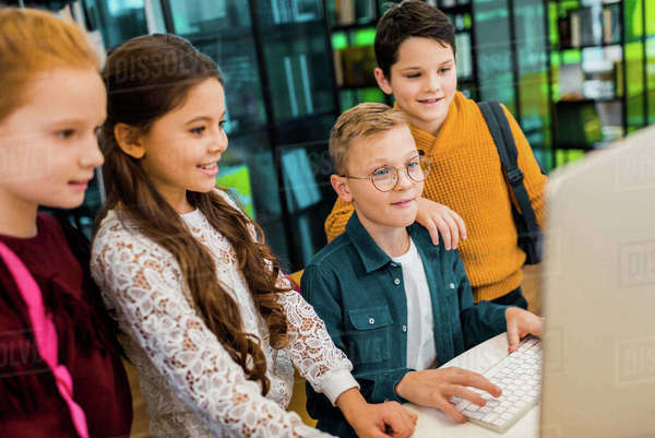 Cute happy schoolkids using desktop computer in library - Stock Photo ...