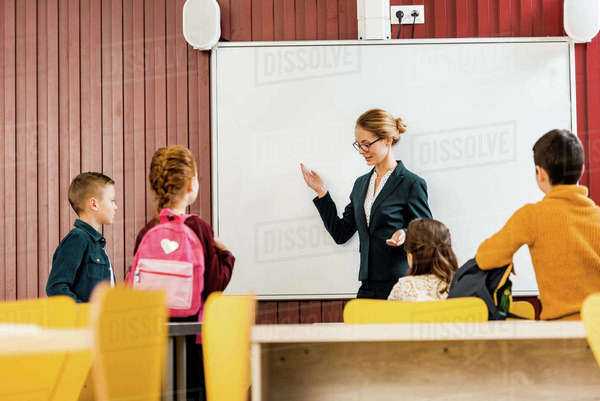 Smiling young teacher making presentation to school children with ...
