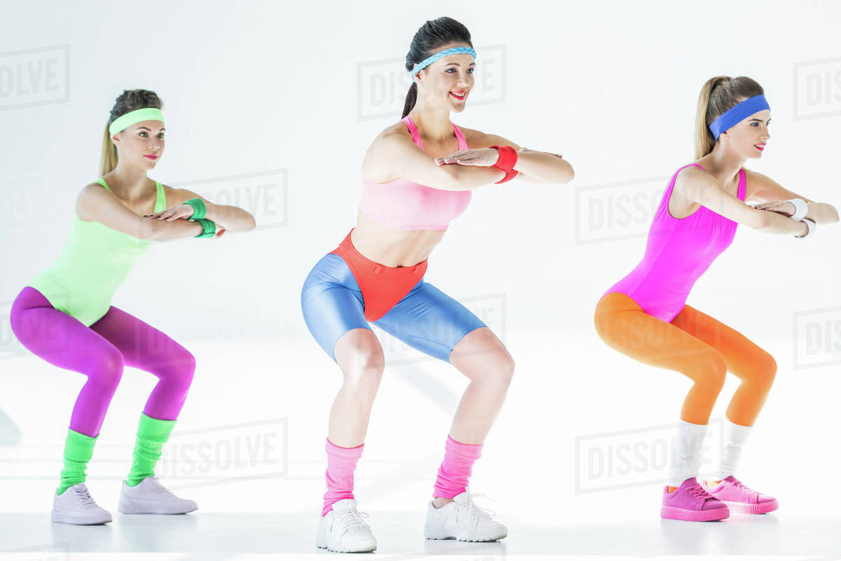 Full length view of sporty smiling girls doing squat on grey - Stock ...