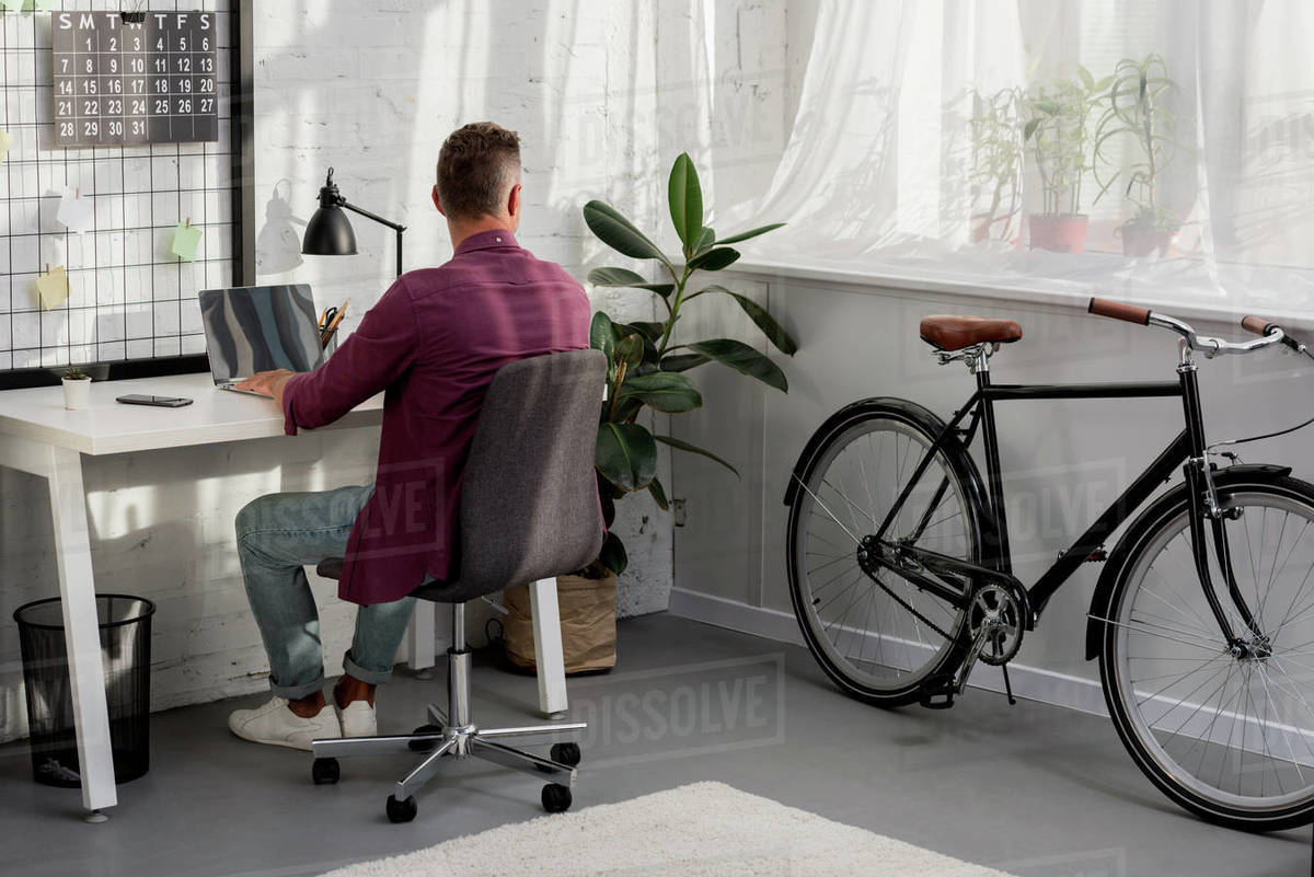 Back view of man sitting at work place and looking out the window at ...