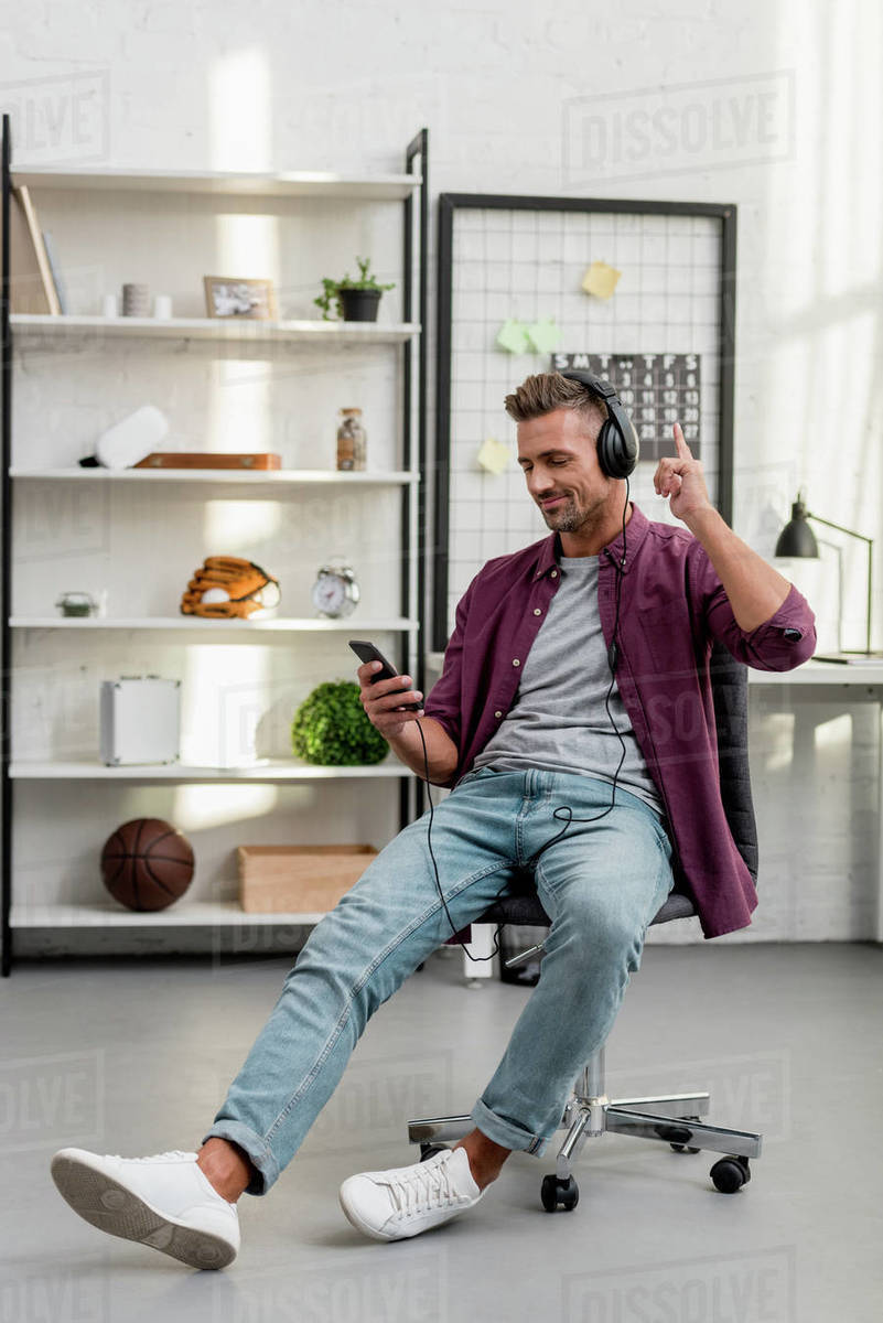 Happy man with headphones listening music and singing while sitting on ...