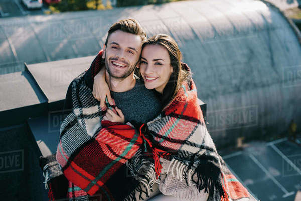 High angle view of beautiful young couple covered in plaid embracing ...