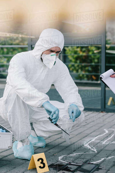 Criminologist in protective suit and latex gloves taking knife into ...