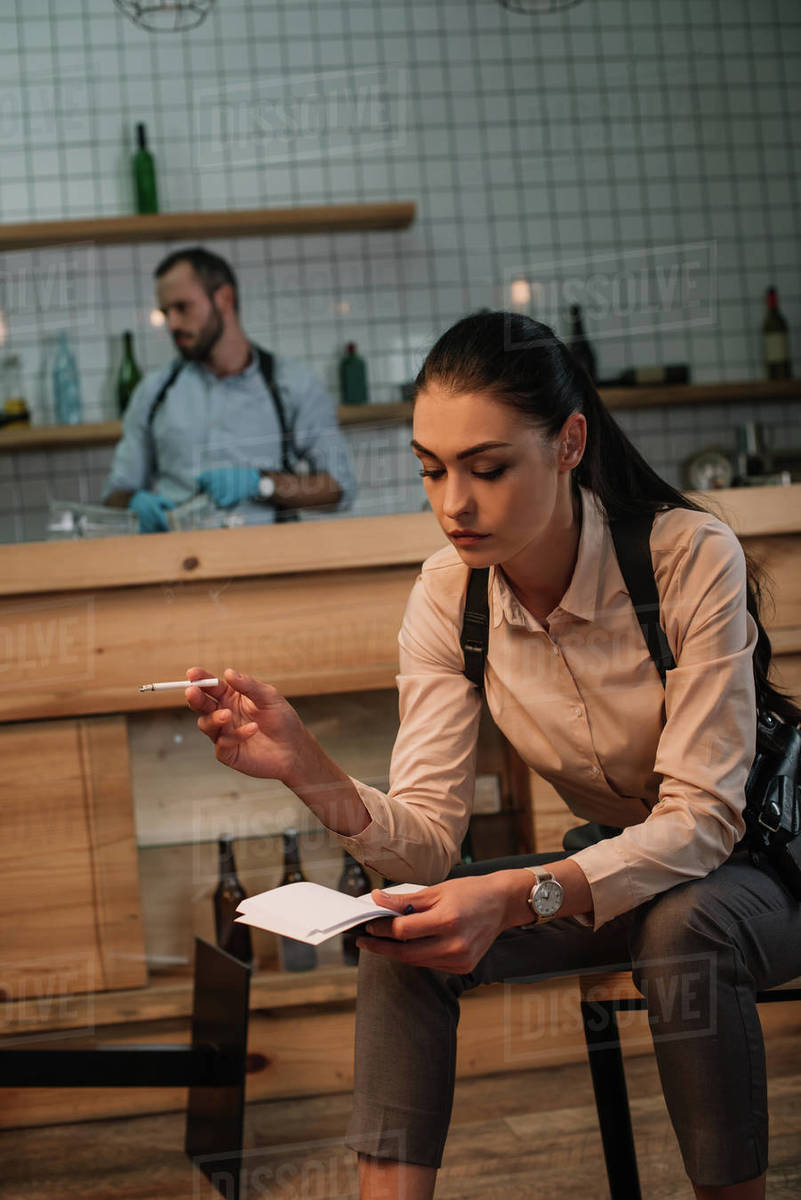 Serious smoking female detective sitting at crime scene with colleague ...