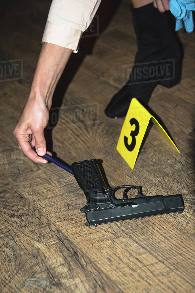 Cropped view of hand examining gun near evidence marker at crime scene ...