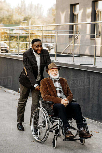 Happy senior disabled man in wheelchair and African American man riding ...