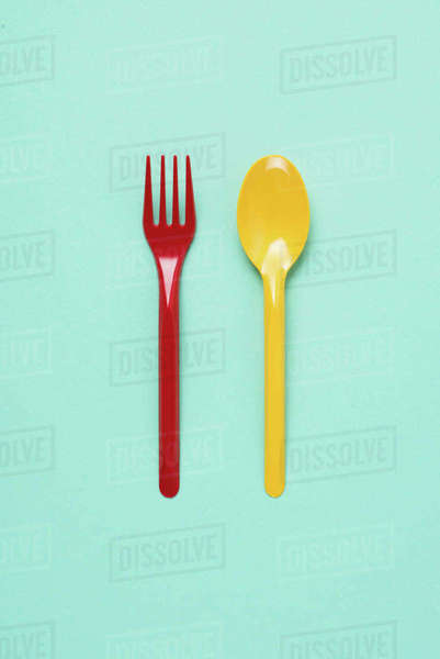 Top view of red plastic fork and yellow spoon on blue background ...