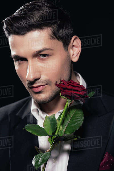 Portrait of handsome man in suit holding red rose isolated on black ...