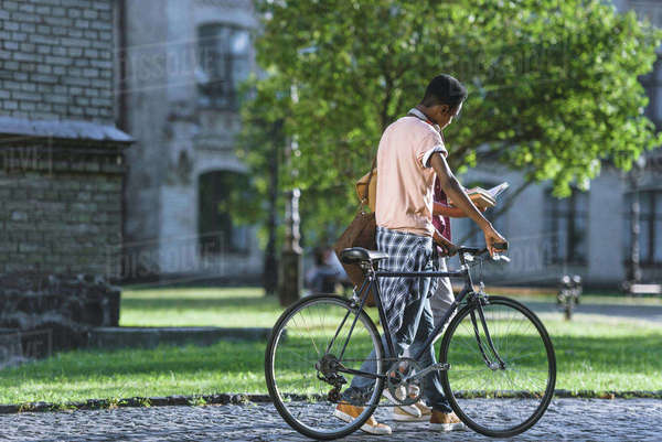 Multicultural young students with bicycle walking together along park ...