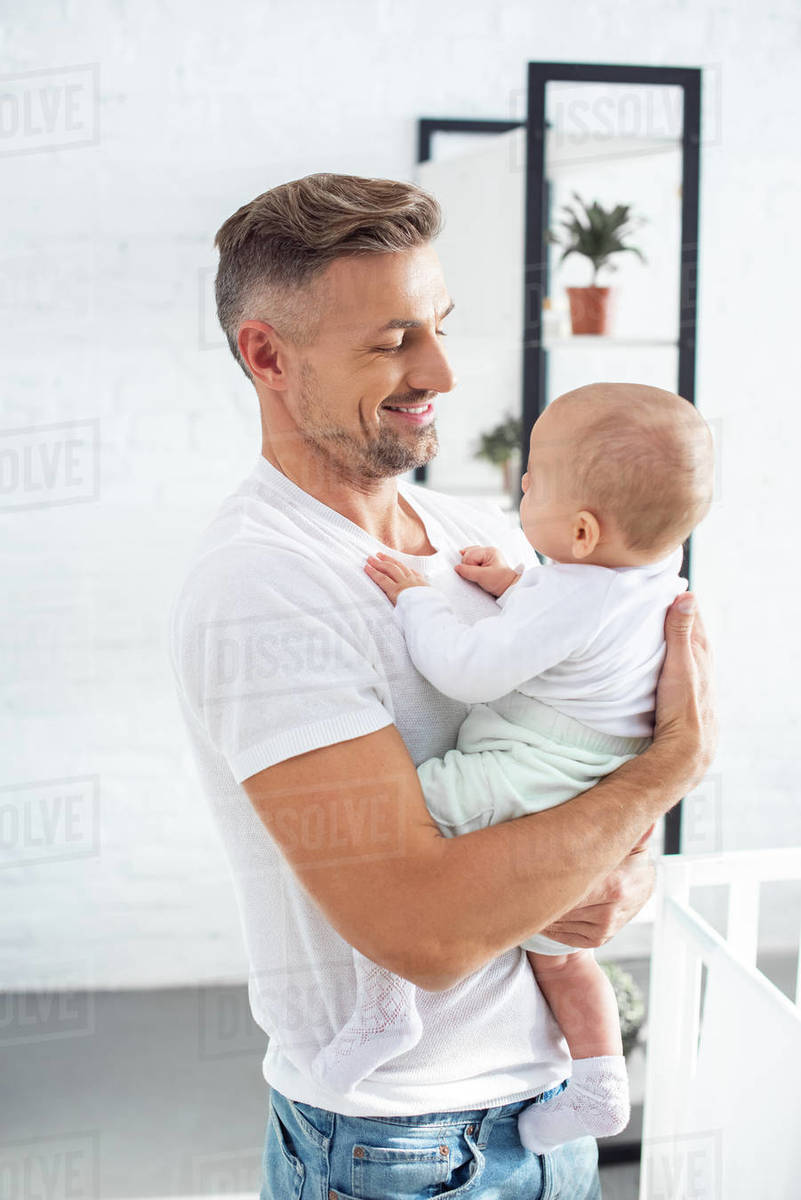 Father looking at baby daughter and smiling at home - Royalty-free ...