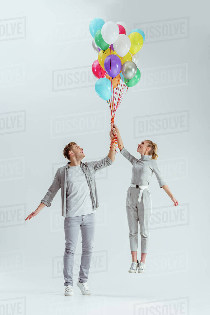 happy couple jumping with bundle of colorful balloons on grey ...