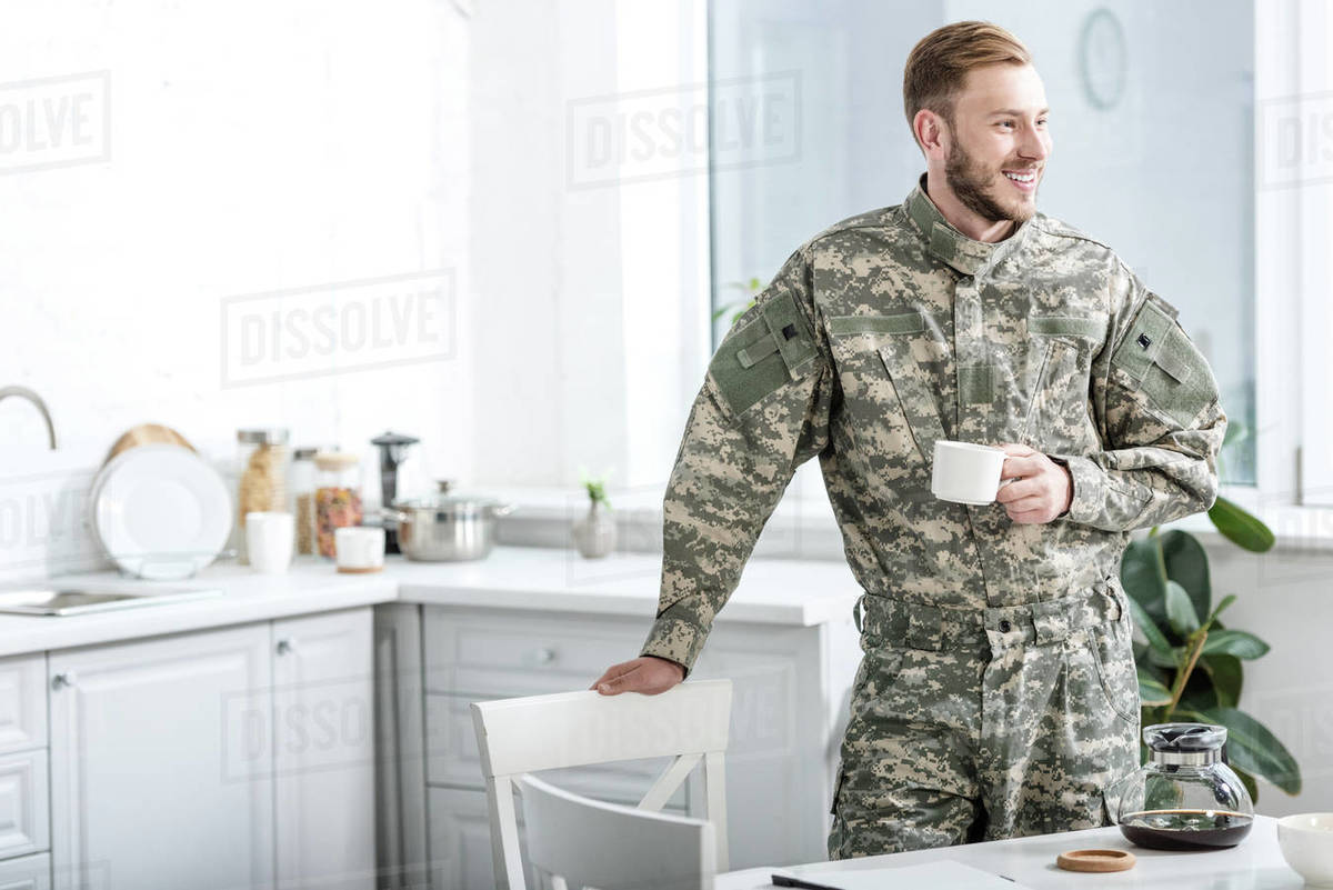 smiling army soldier holding cup of coffee in kitchen - Royalty-free ...
