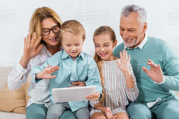 Grandparents and grandchildren waving by hands while having video call ...