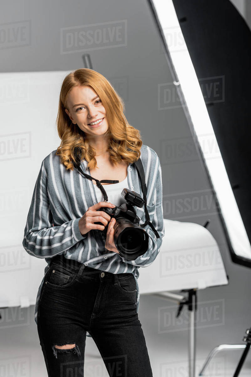 Beautiful young female photographer smiling at camera in photo studio ...