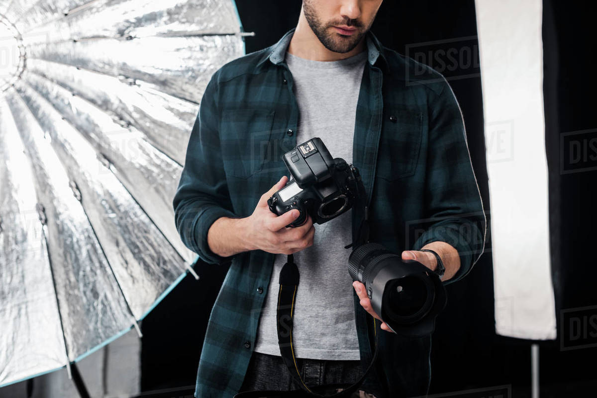 Cropped shot of young photographer holding photo camera and lens in ...
