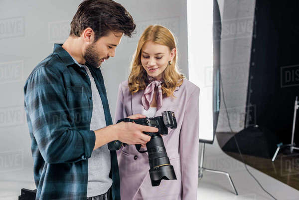 Handsome young photographer and smiling female model using photo camera ...