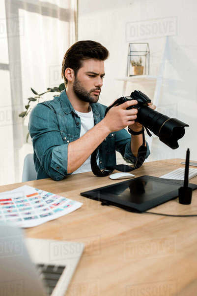 Handsome young photographer using camera at workplace - Stock Photo ...