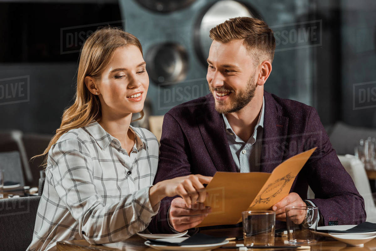 Woman pointing at something while young adult couple looking in menu to ...