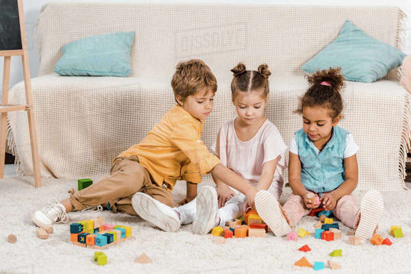 Adorable little ethnic children playing with colorful cubes on carpet ...