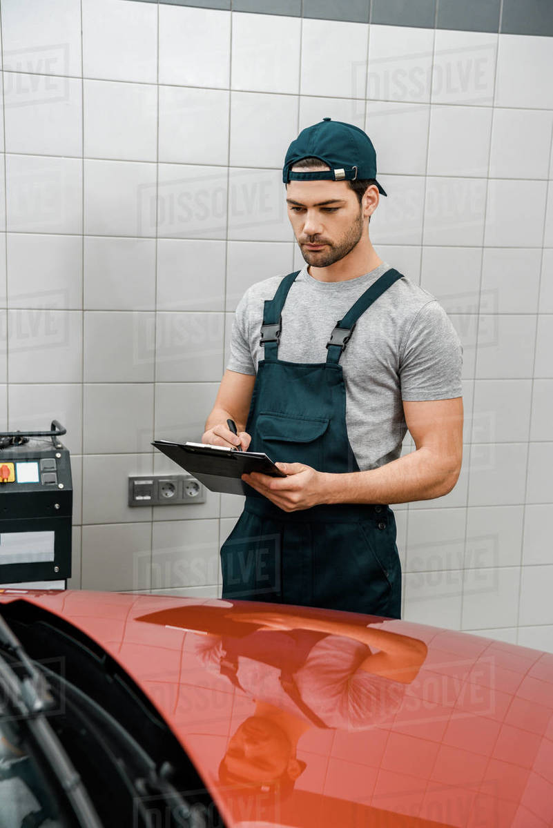 Focused auto mechanic with notepad examining new car at auto repair ...