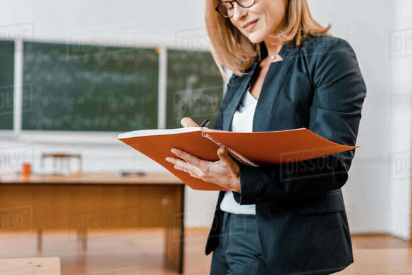 Cropped view of female teacher in formal wear writing in notebook in ...