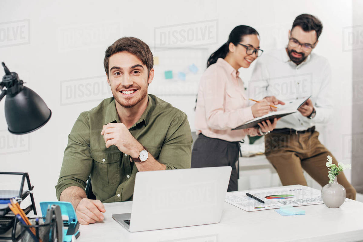 Selective focus of male office manager sitting and smiling with ...