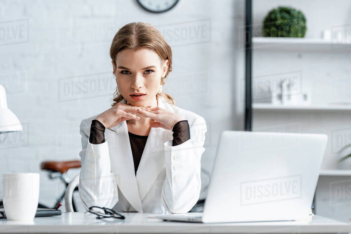 Businesswoman in white formal wear with folded hands sitting at ...