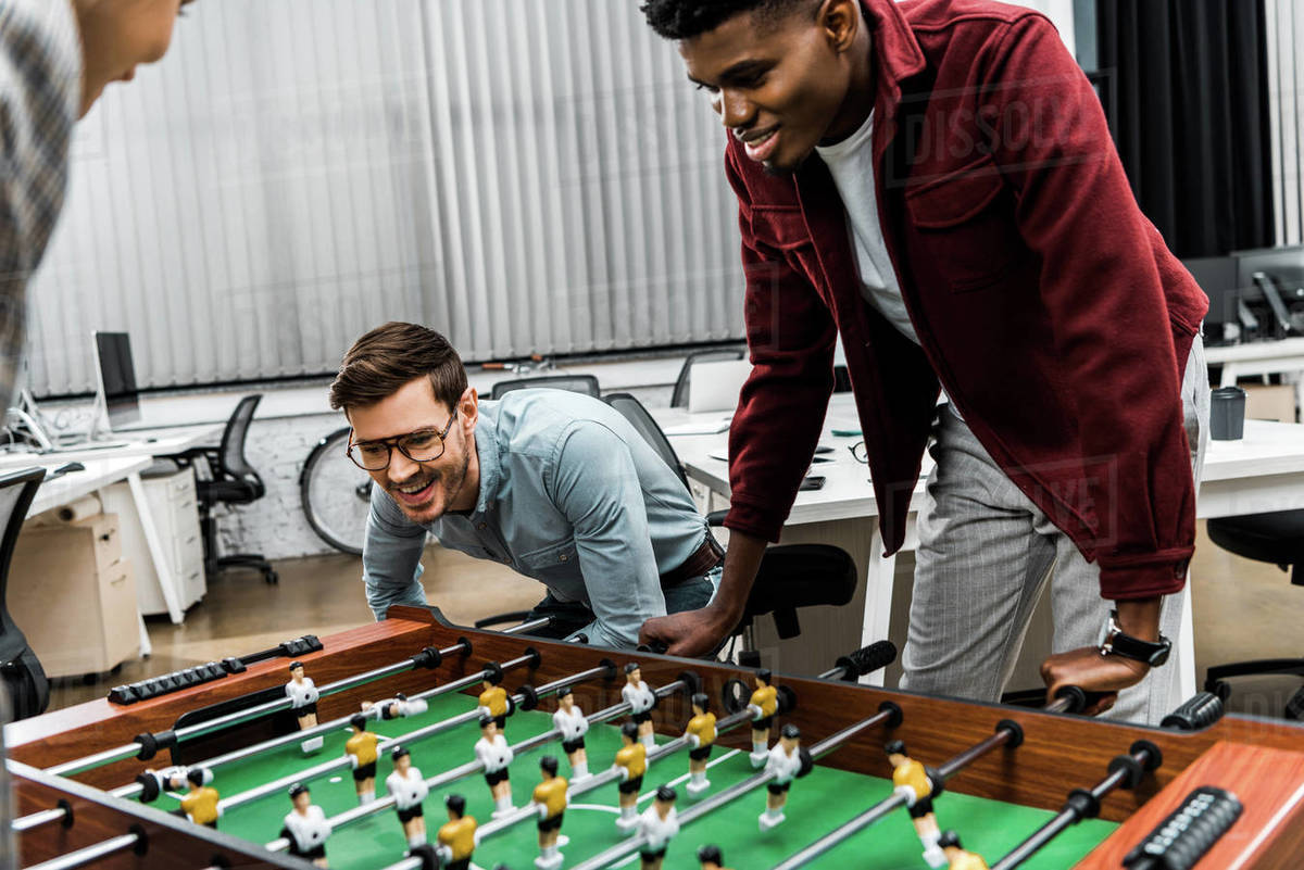 Smiling multicultural businessmen playing table football in office ...